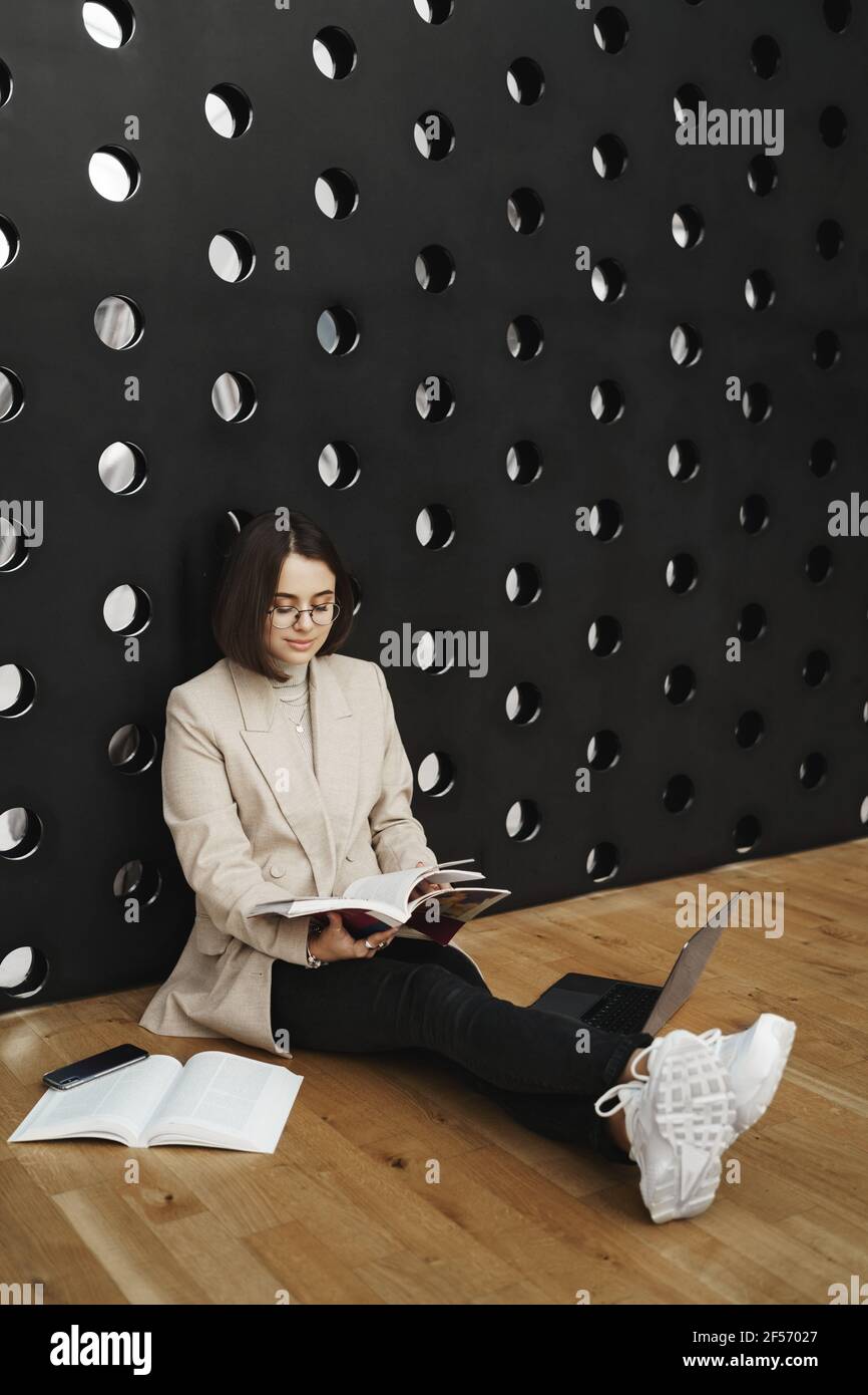 Vertical portrait of smart pretty young woman studying on floor with ...