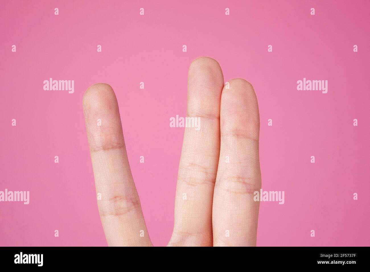 Closeup of a person showing three fingers against a light pink ...