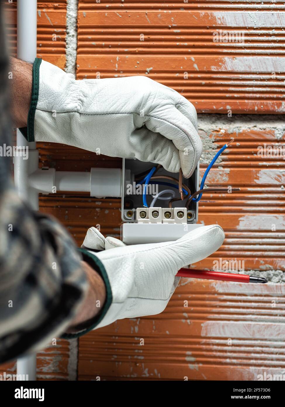 Electrician worker at work inserts the electrical cable into the clamp ...