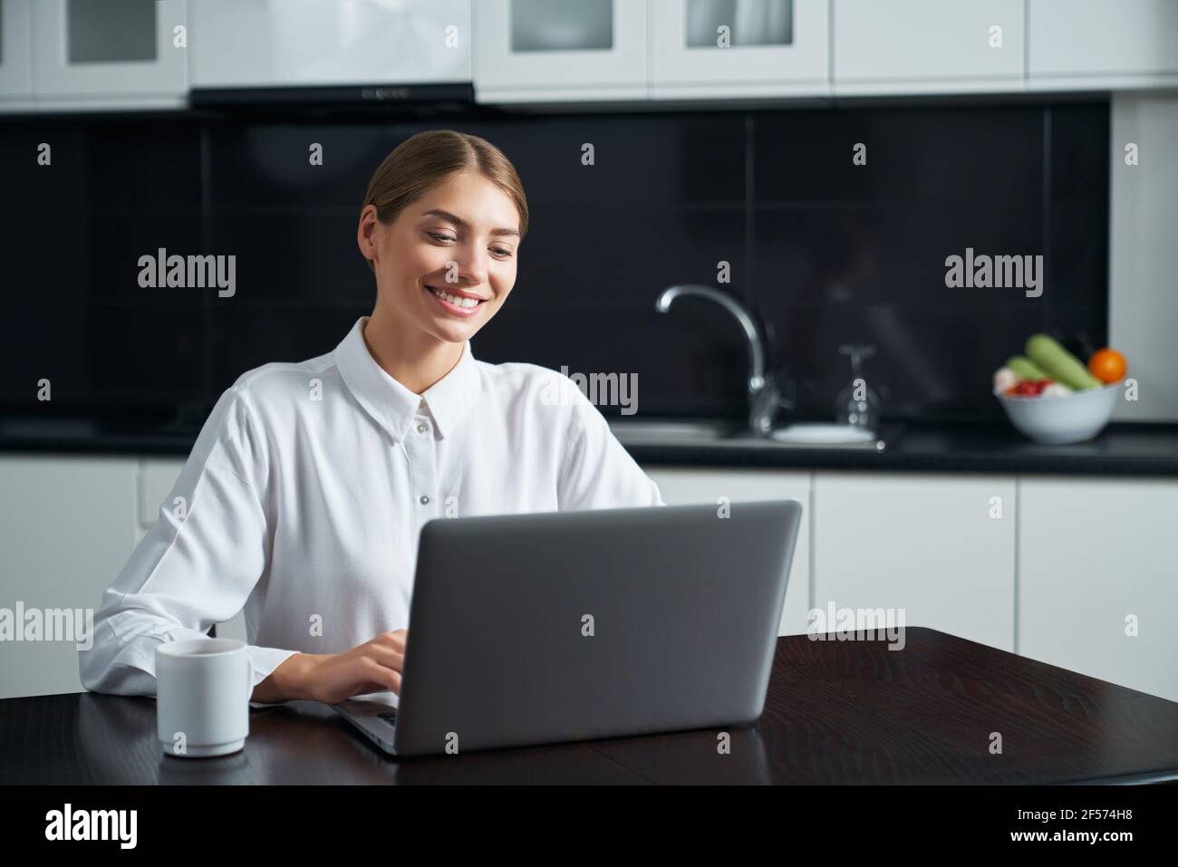 Positive woman in casual wear using modern laptop while staying at home ...