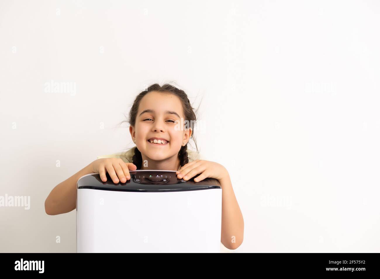 Cute little girl standing breathing at air purifier. Clean air concept ...
