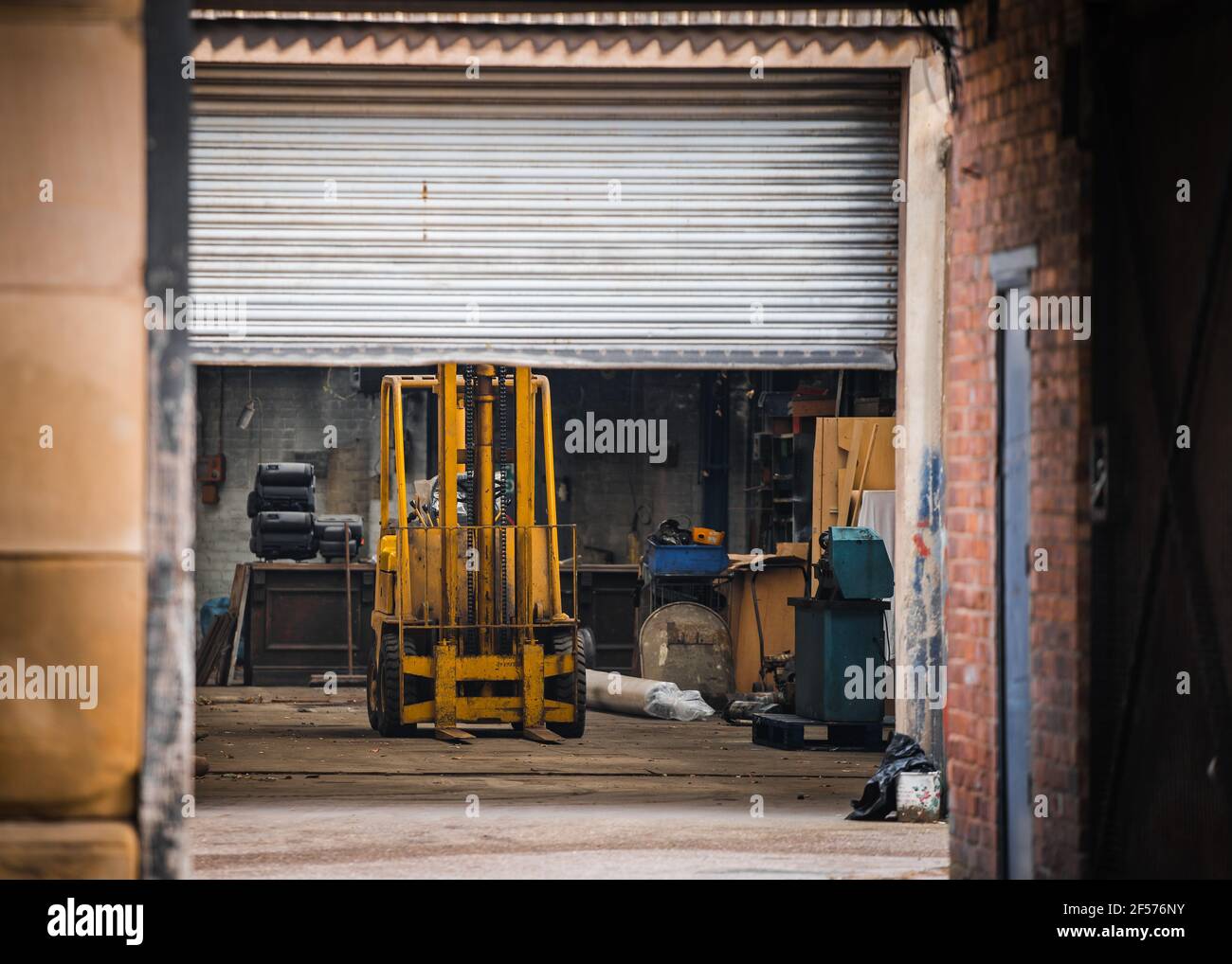 Old yellow fork lift truck parked in garage with roller shutter door ...