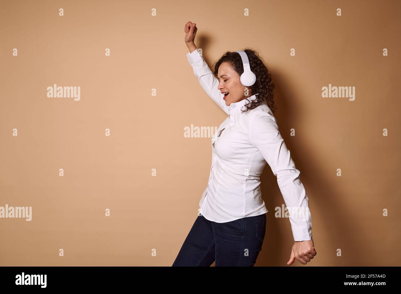 Happy curly haired woman dancing with outstretched arms on beige ...