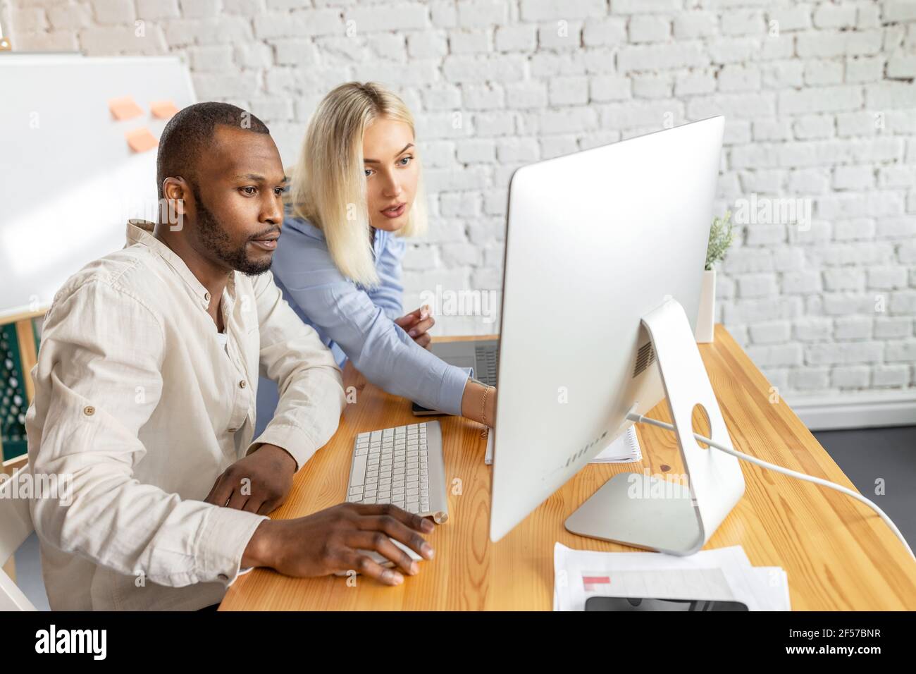 Focused young adult colleagues sitting at the desk, using computer ...