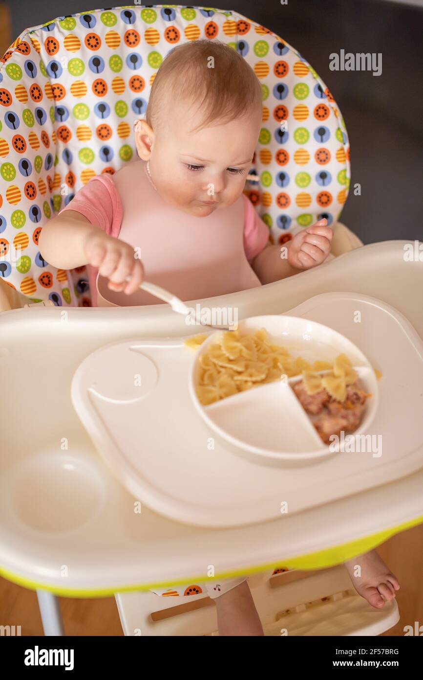 One year old girl having balanced meal in baby eating chair, healthy ...