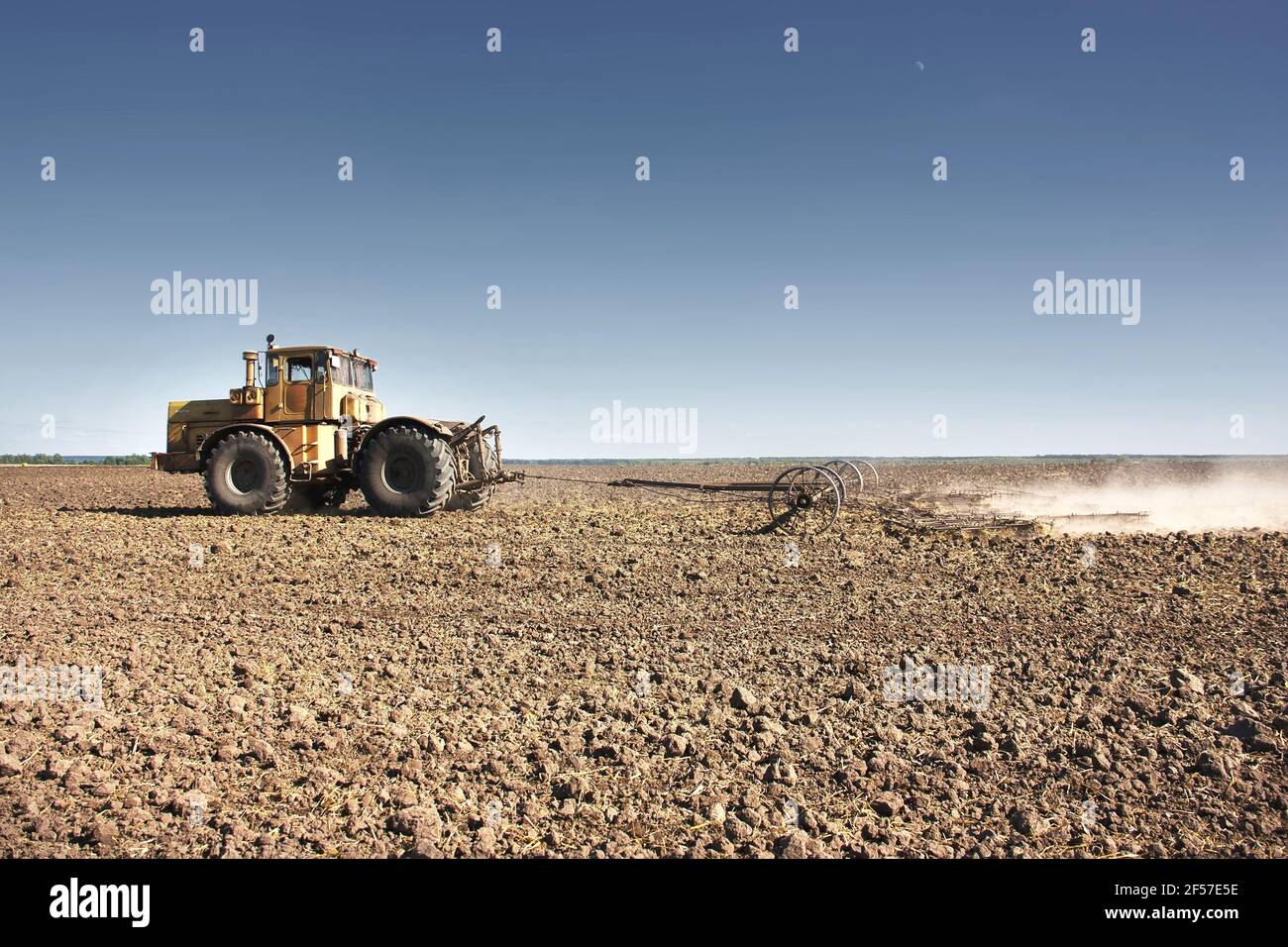 Big yellow tractor equipped with harrow working on the field Stock ...