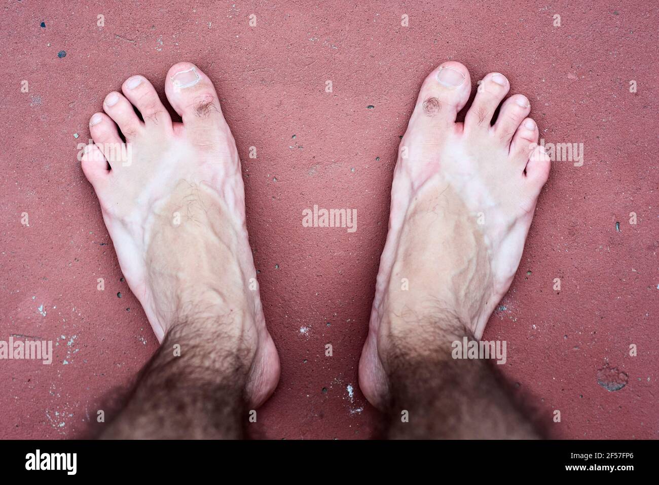 Close up from above of caucasian young man's bare feet standing on red ...