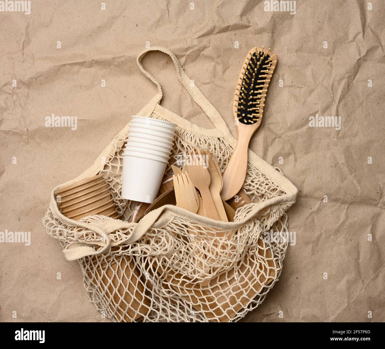 white string bag with disposable paper dishes and wooden forks on brown ...
