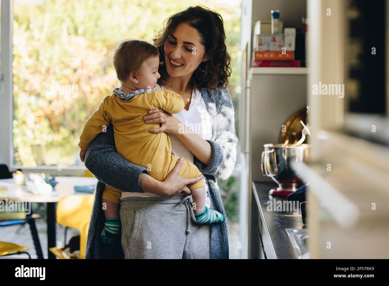 Mother with baby in kitchen. Woman carrying her son standing in kitchen ...