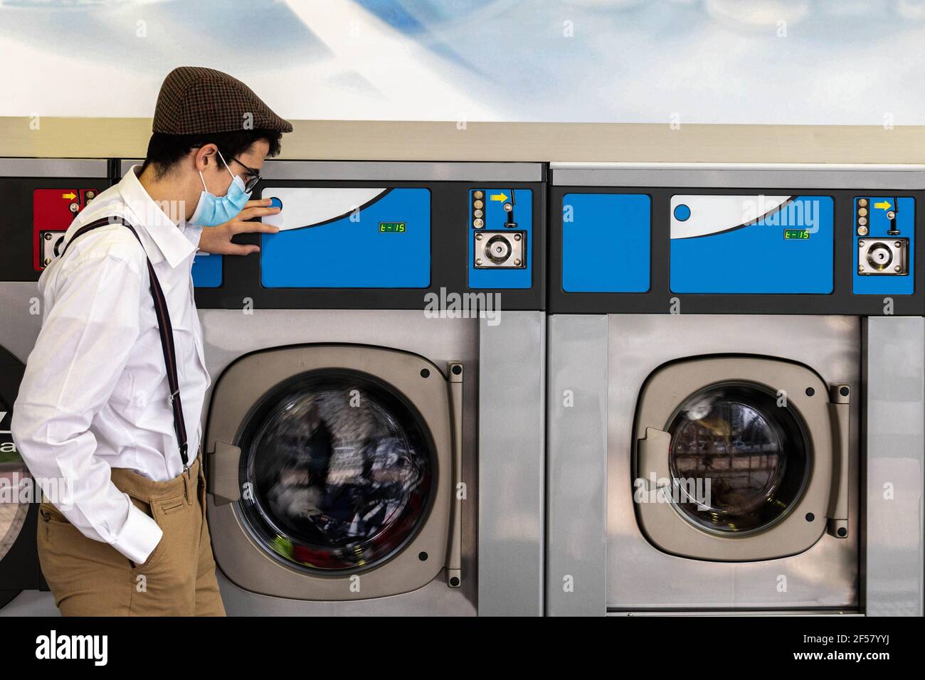 teenager with mask and cap observing how industrial washing machines ...