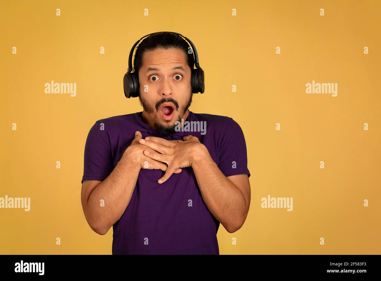 Young man with surprised face listening to music using headphones ...