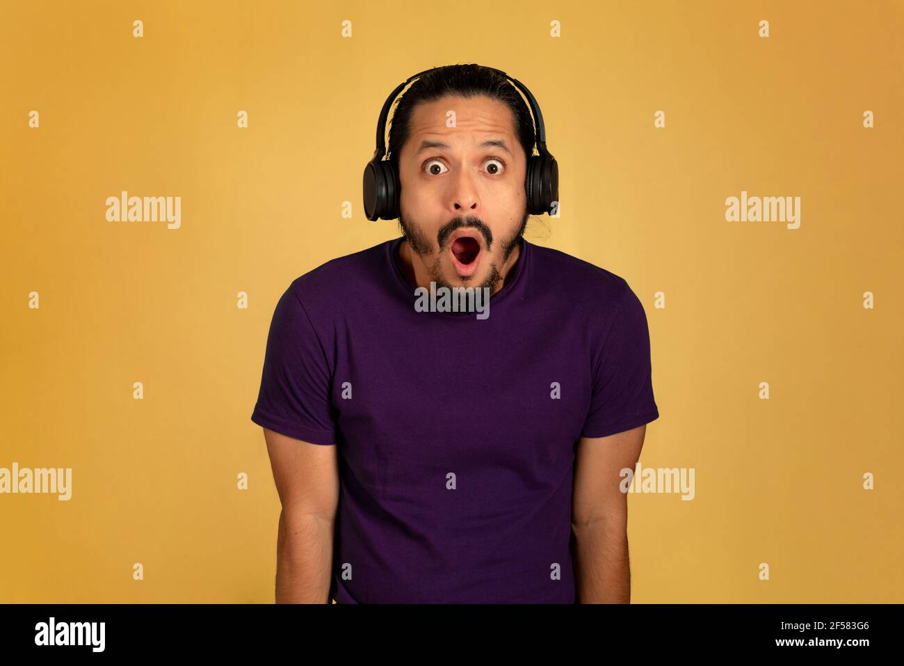 Young man with surprised face listening to music using headphones ...