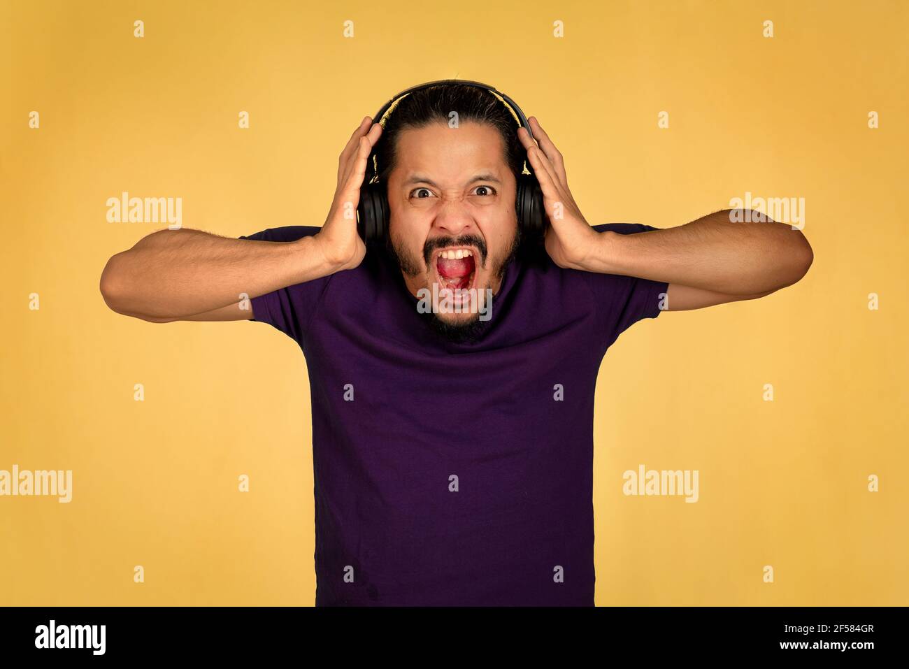 Young man screaming and listening music using headphones and playing ...