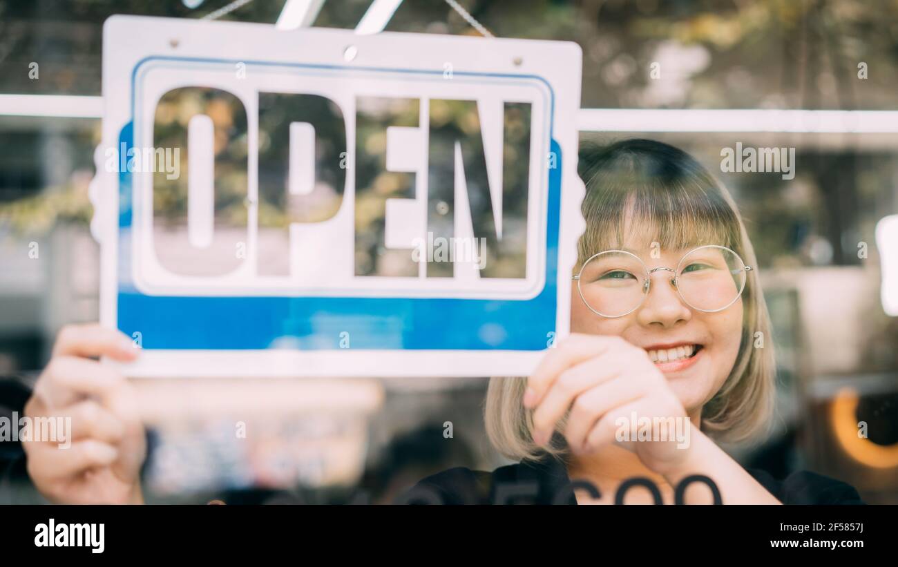 Young Asian woman hanging open sign by glass window. Female shop owner ...