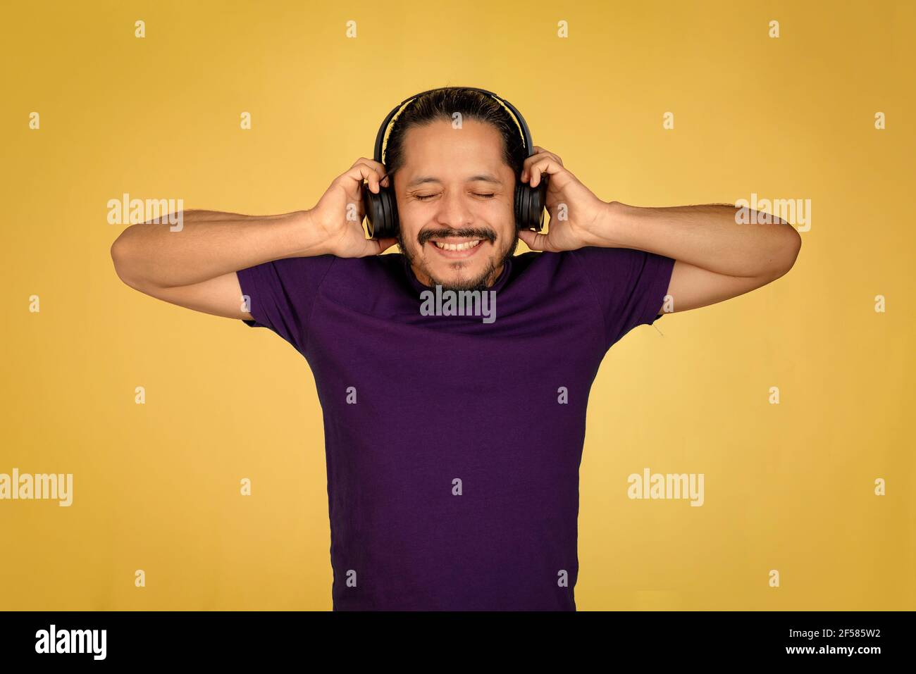 Young man with a smily face listening to music using headphones. Yellow ...