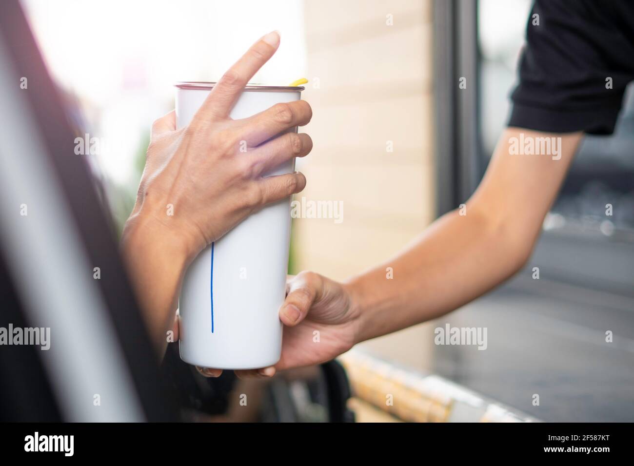 Hand in the car is picking up a personal cup of coffee from the ...