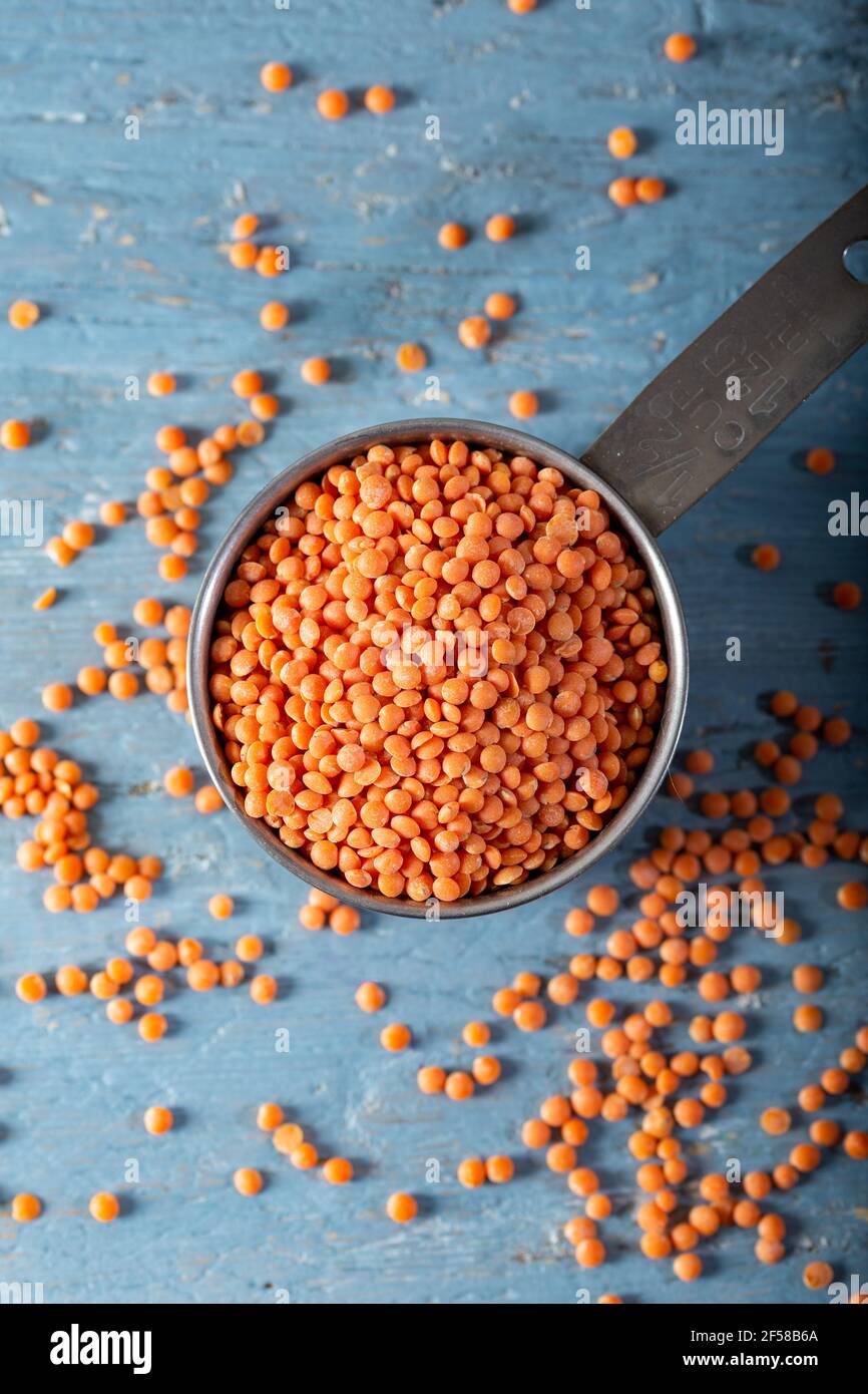 Red lentils in a metal measuring cup on a blue natural wood background ...