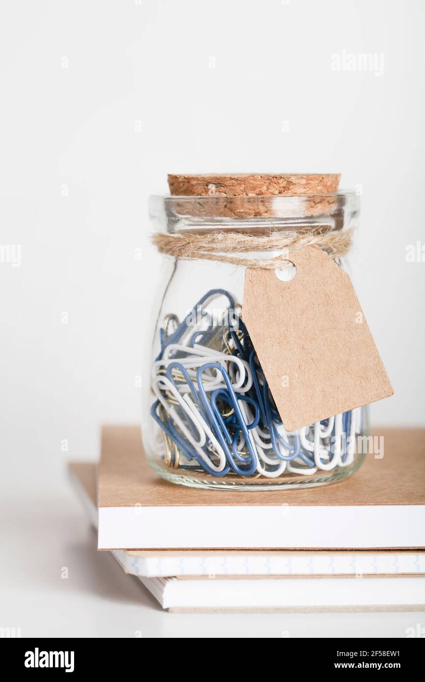 paper clips in glass jar with blank paper tag on stack of notepads ...