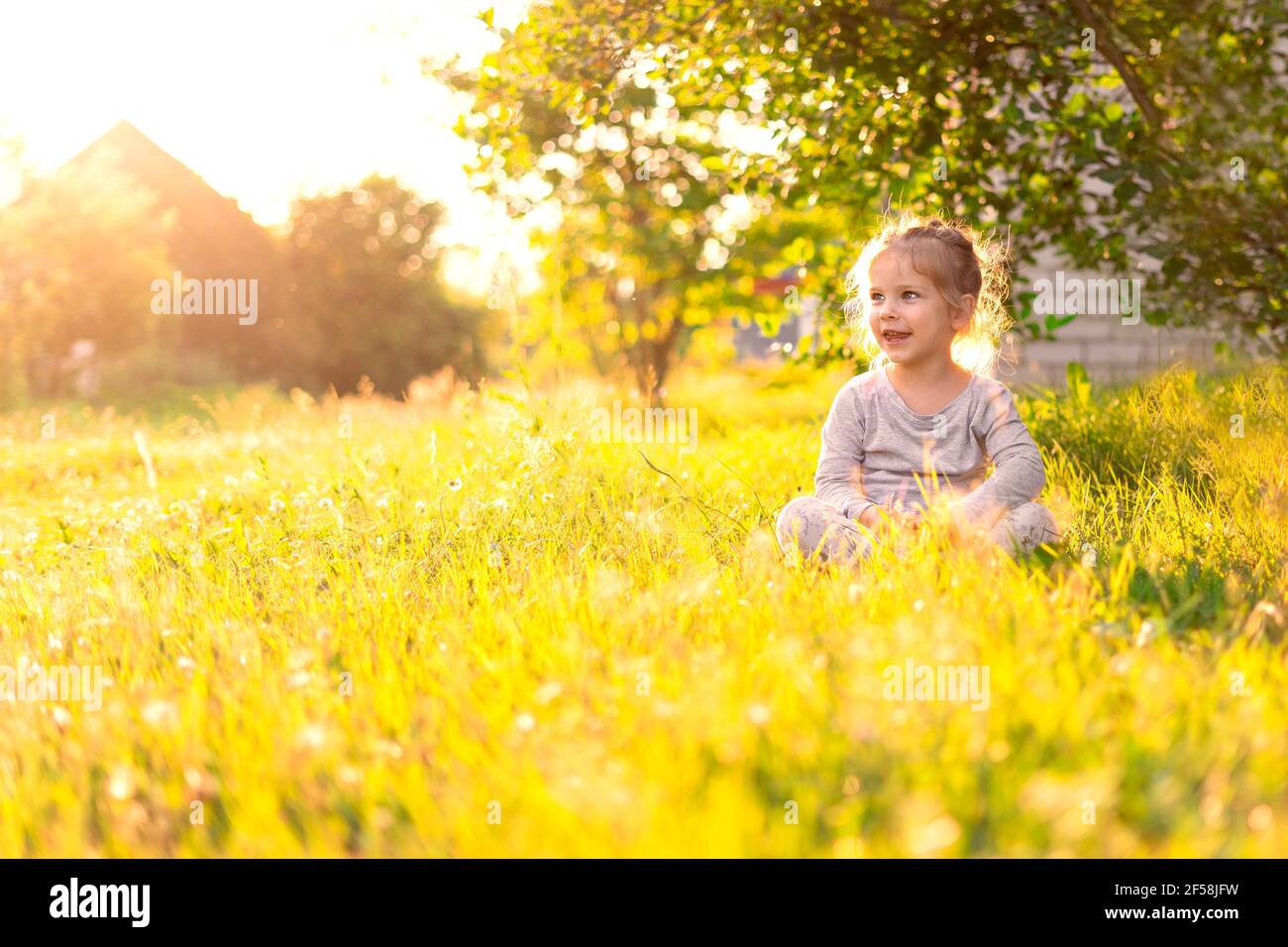 cute little girl smiling sitting in the grass at sunset. backlight of ...