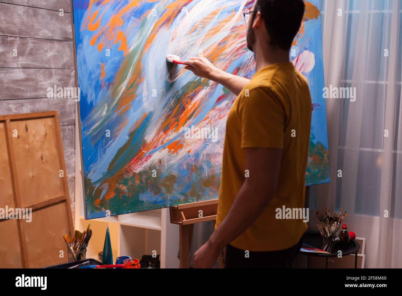 Successful young painter in art studio painting on large canvas. Modern ...