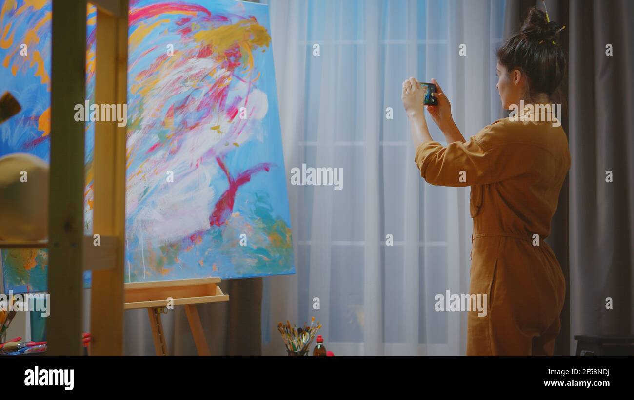 Innovative woman painter taking photo of her masterpiece in art studio ...