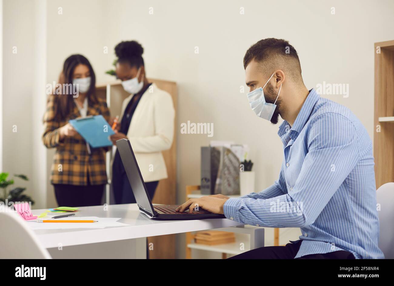 Man employee in face medical mask working on laptop in office after ...