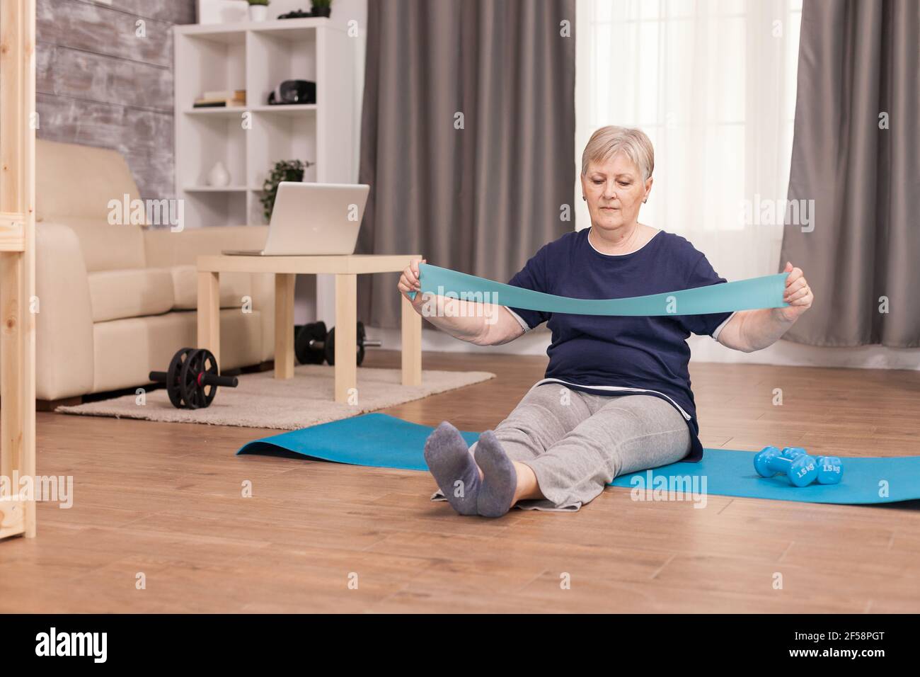 Active grandma using resistance band sitting on yoga mat at home. Old ...