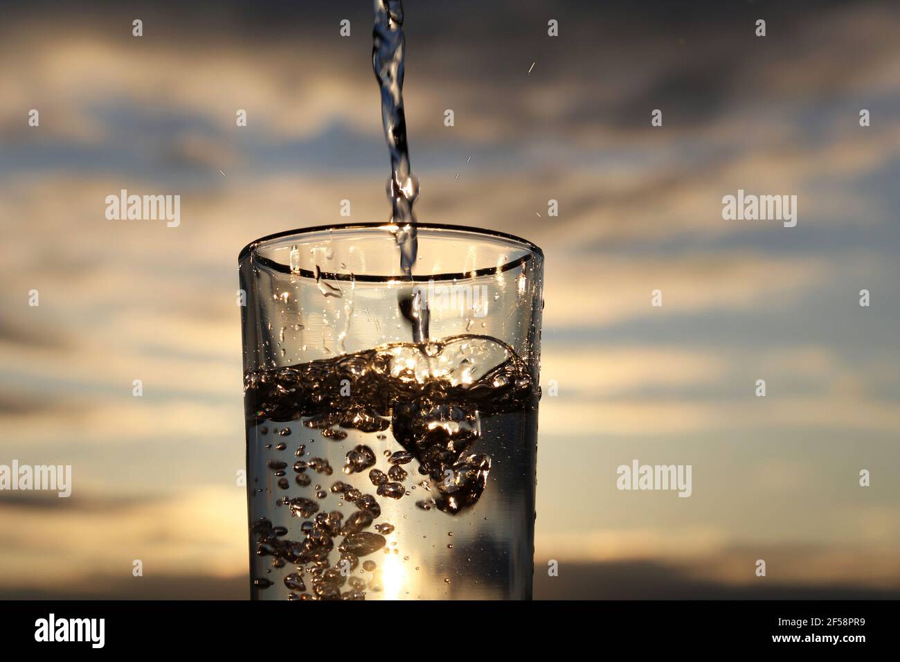 Clean water pouring into drinking glass on sunset blurred background ...