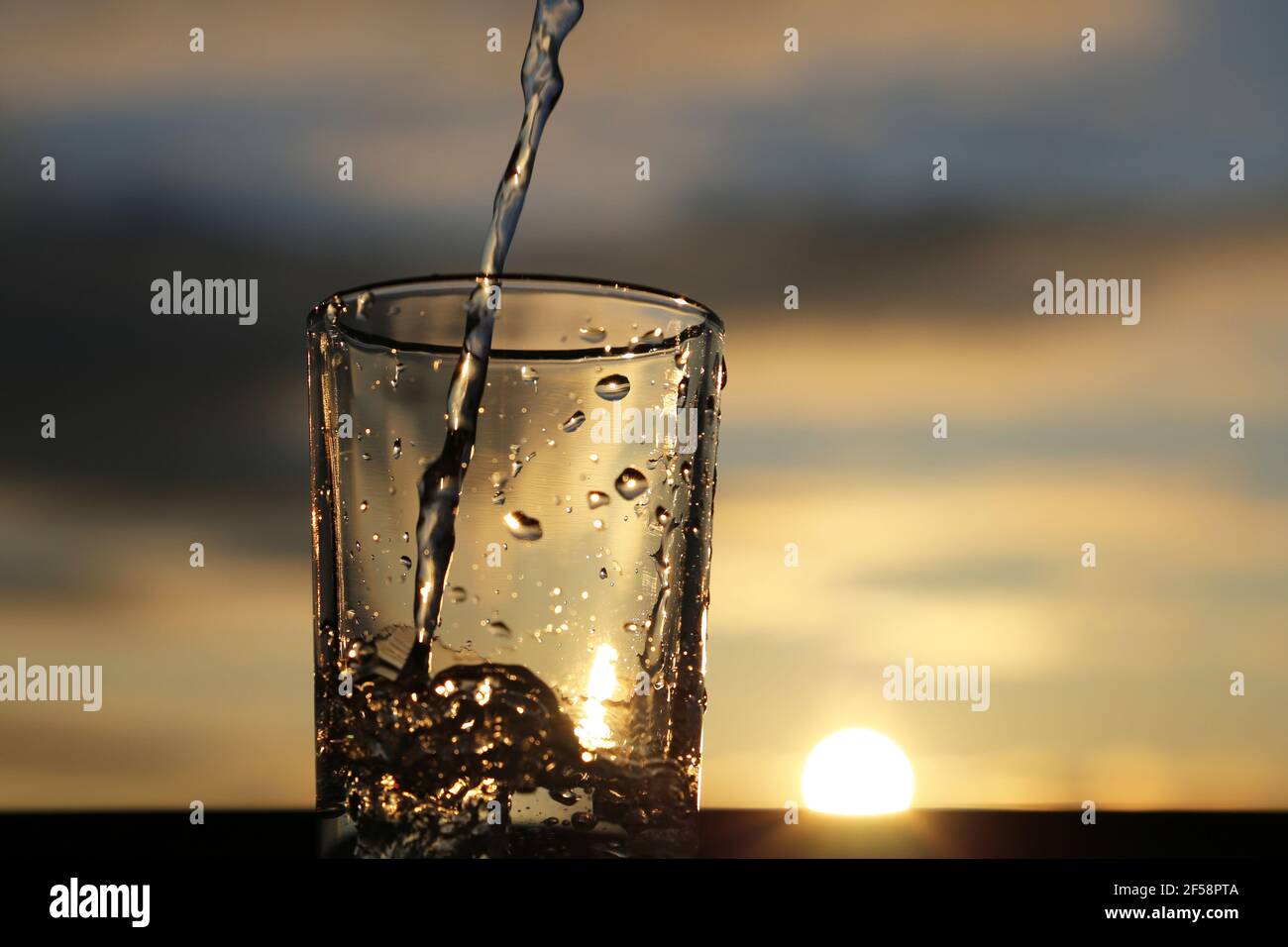 Pouring clean water into drinking glass on evening sun background ...