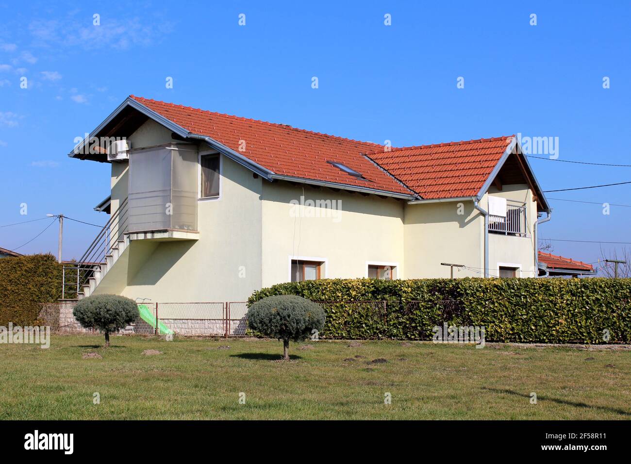 Curiously looking newly built suburban family house with new light yellow facade and bright red ...