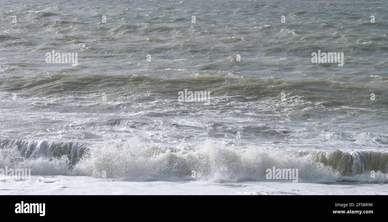 Waves of a choppy sea seen braking on the shoreline of an English beach ...