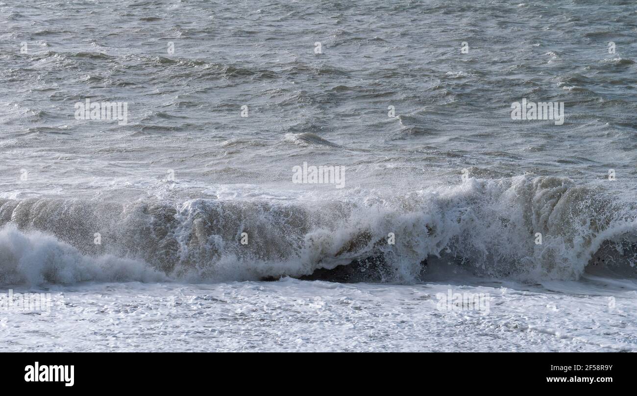 Waves of a choppy sea seen braking on the shoreline of an English beach ...