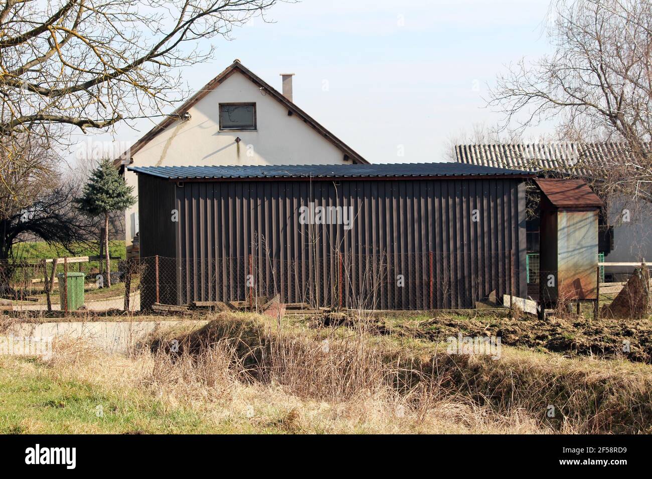 Elongated garage covered with dark corrugated metal protection in suburban family house backyard ...