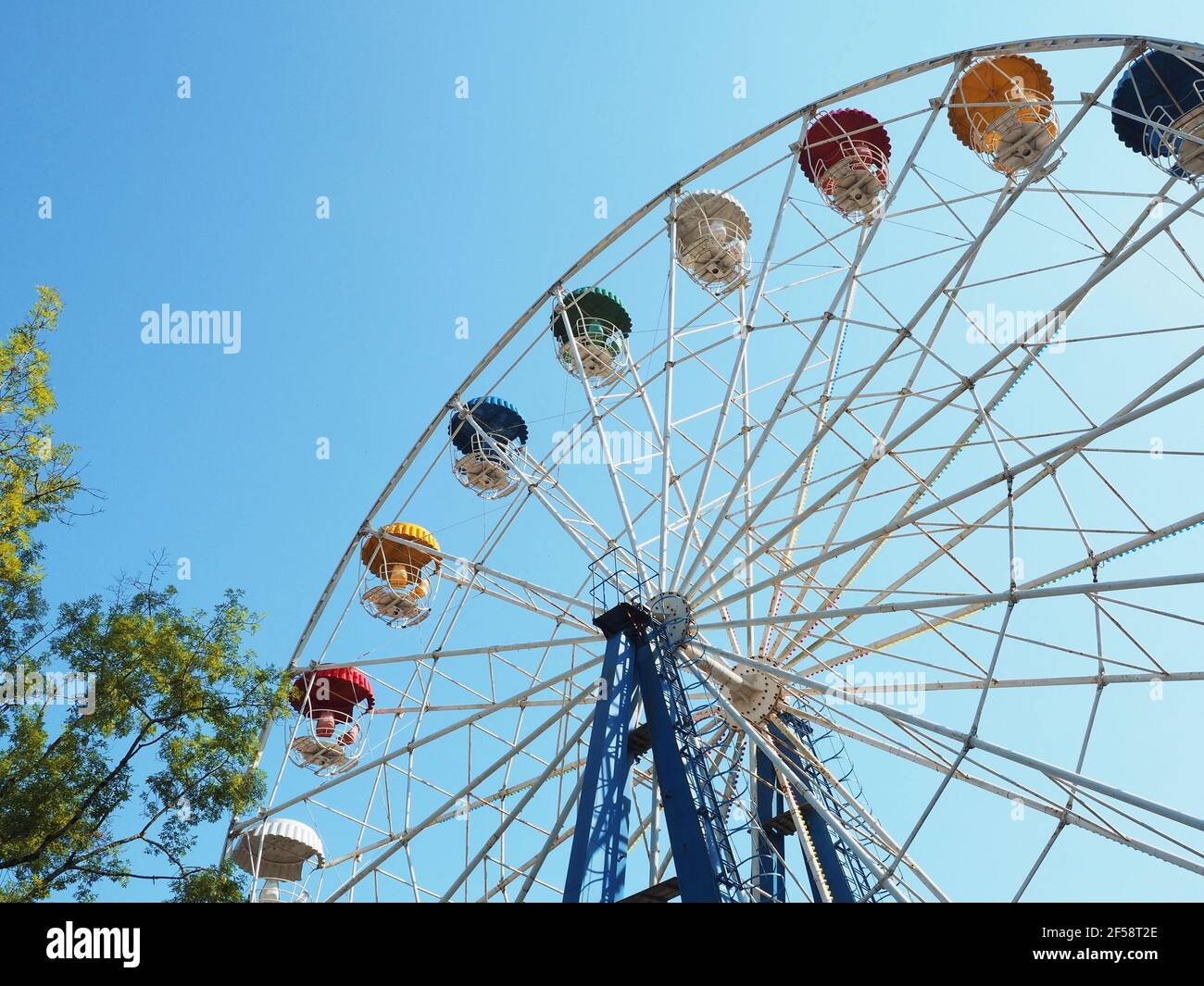 Ferris wheel with multi-colored booths against clear blue sky. Bottom ...