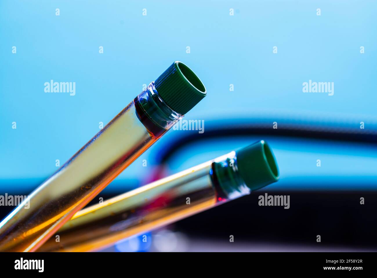 Two chemical test tubes with closed lids with orange liquid on a blue ...