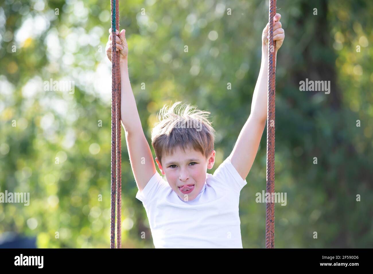 The boy rides on a swing in the summer against the backdrop of greenery ...