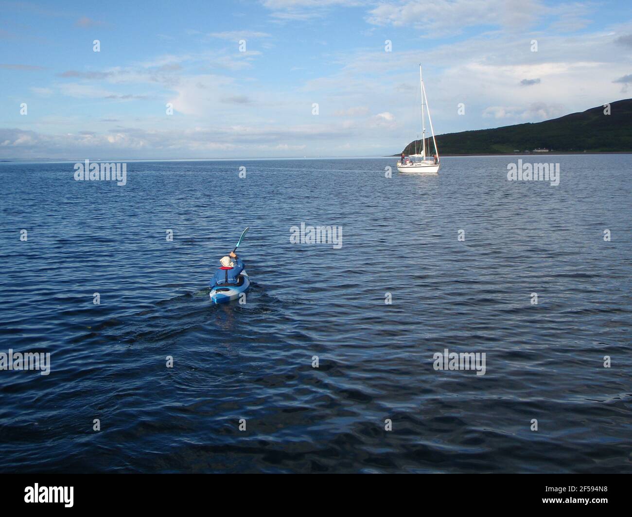 Kayak paddling out to sea towards a yacht & distant land Stock Photo ...