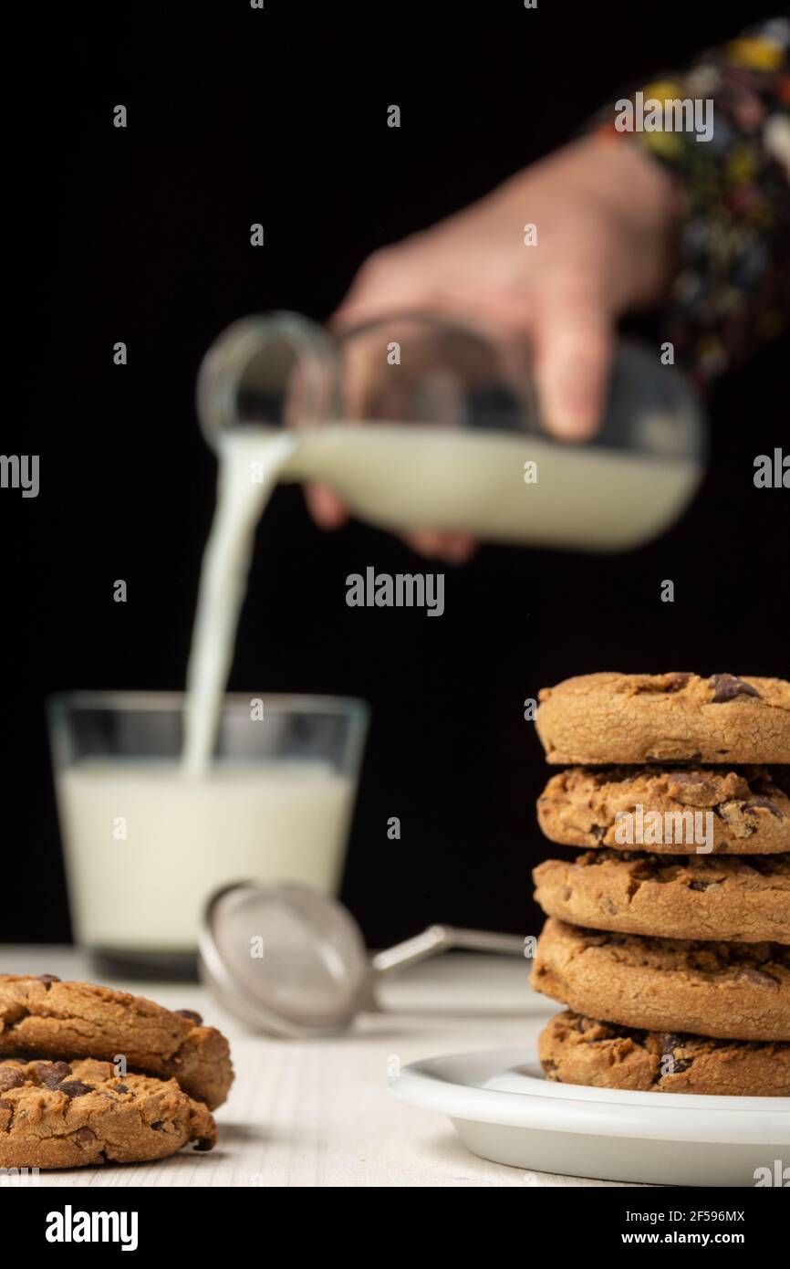 Close-up of stack of chocolate cookies and woman's hand pouring milk ...