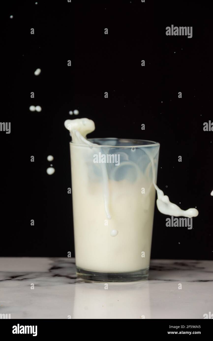 Close-up of glass of milk, with liquid falling, on white marble table ...