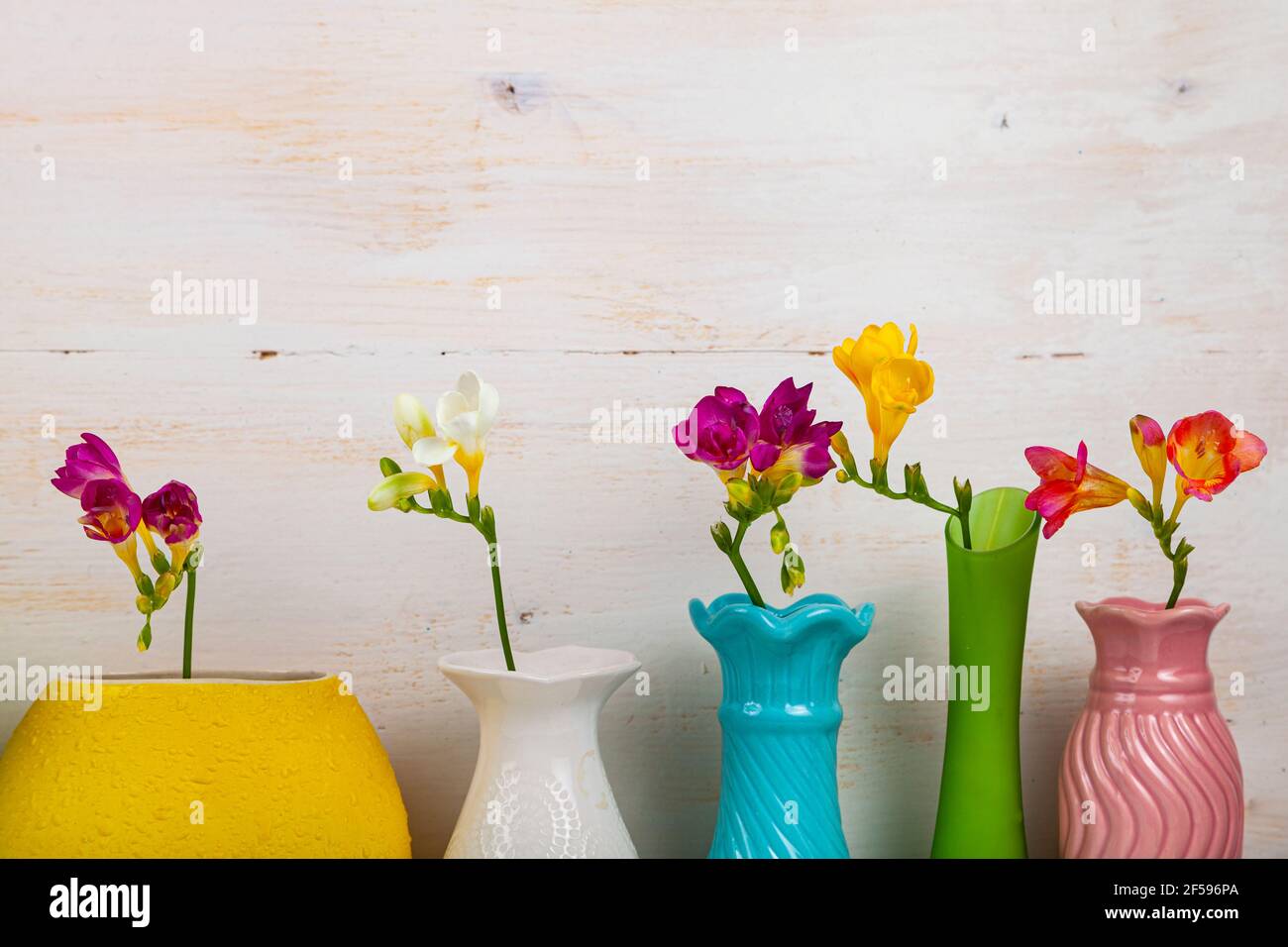 Beautiful flowers. Freesias in multi-colored vases on a white wooden ...