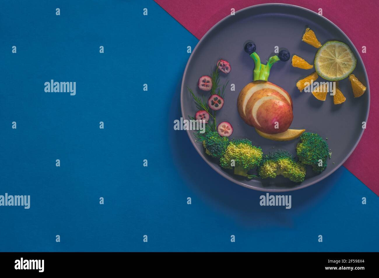 shape of snail and sun from colorful vegetables on the plate with blue ...
