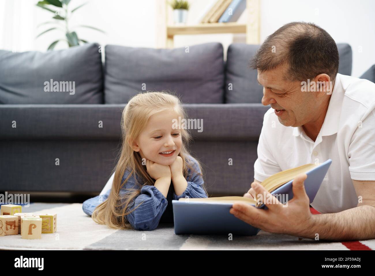 Grandfather reading a book to his little graddaughter in living room ...