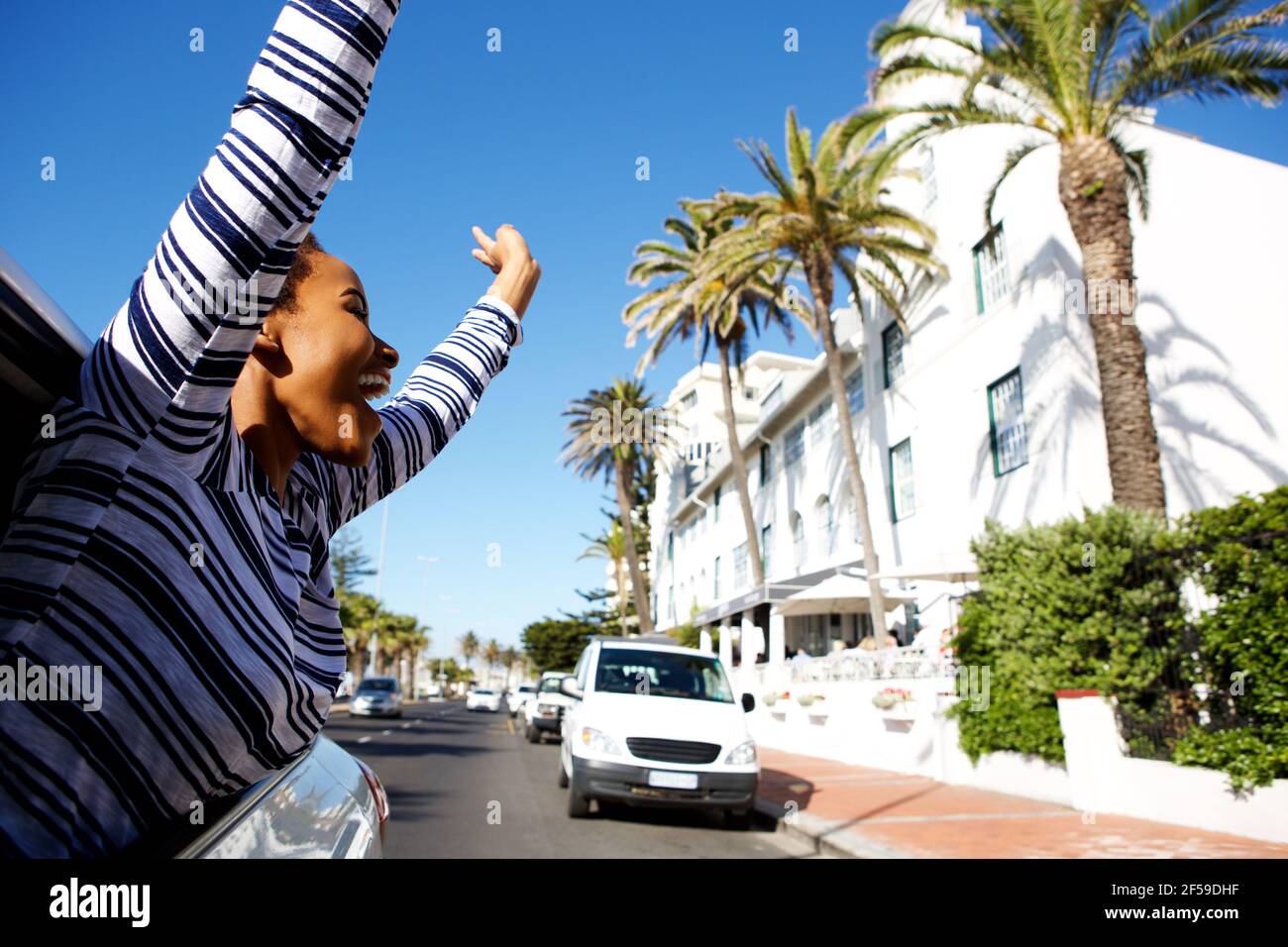 Portrait of happy young black woman hanging outside car window with ...