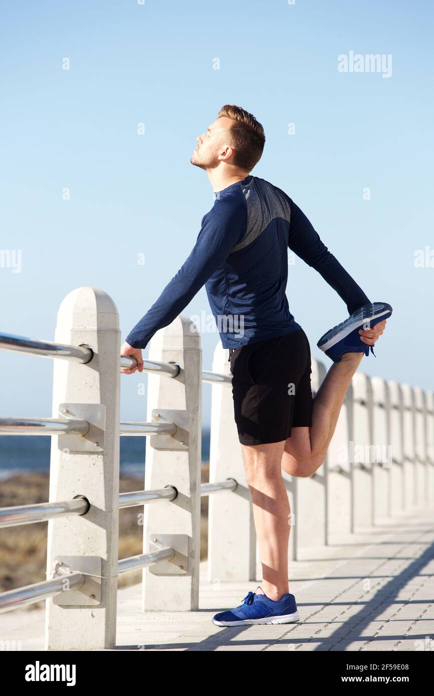 Portrait of active young man standing on one legs stretching exercise ...