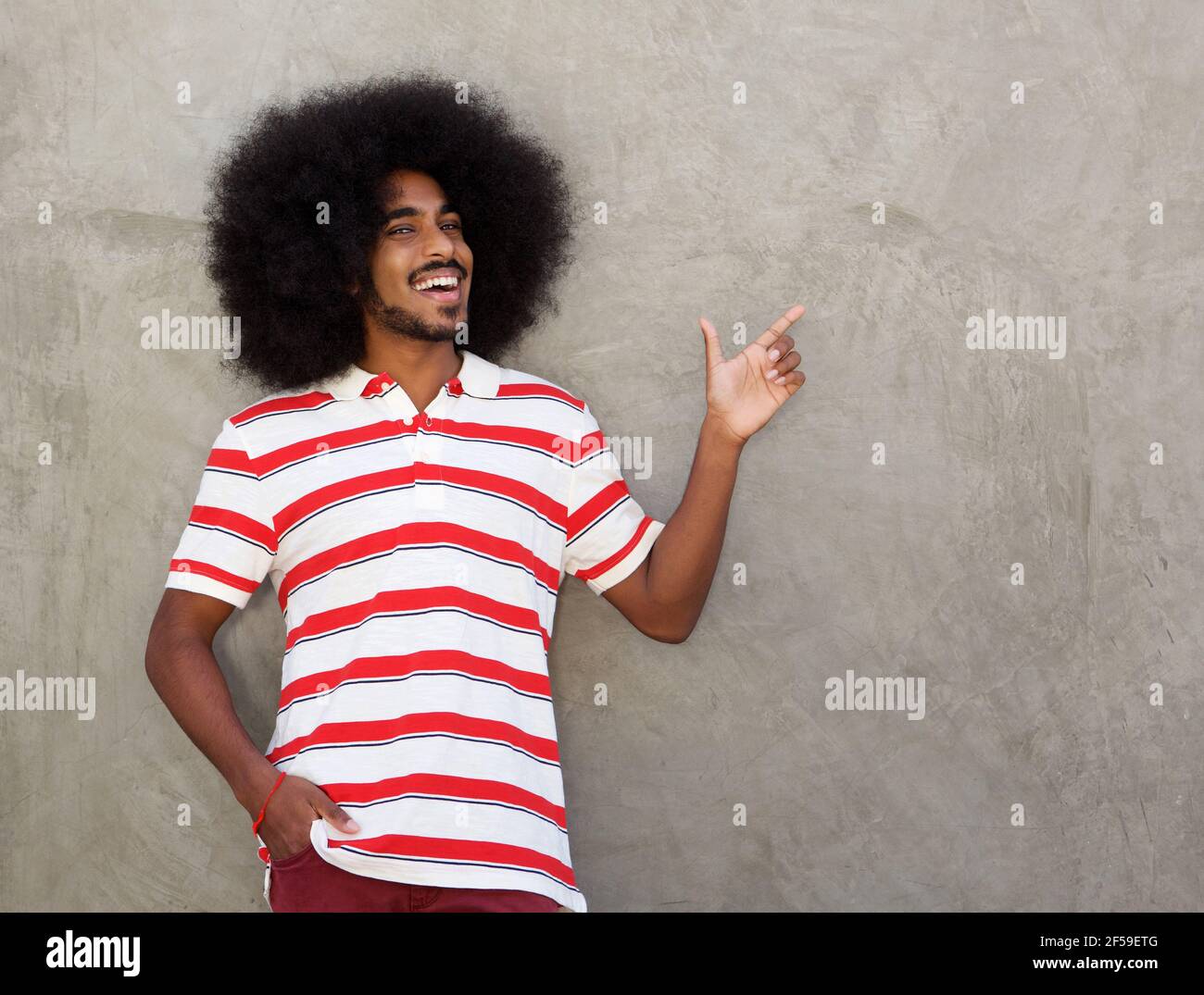 Portrait of smiling man by wall with hand outstretched pointing finger ...