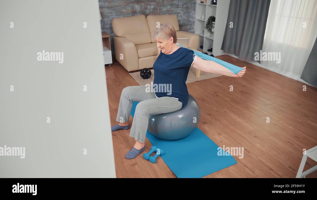 Senior woman sitting on balance ball training with resistance band. Old ...