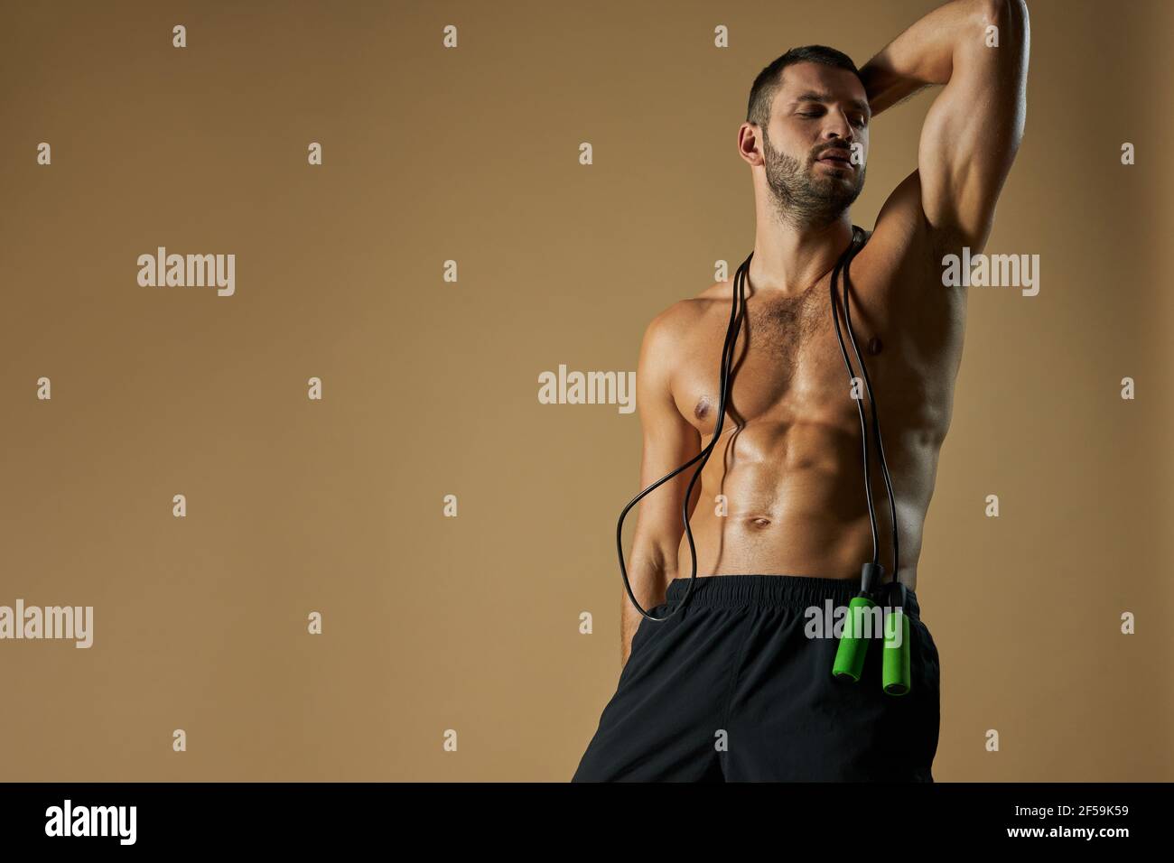 Focused adorable sportsman in black shorts looking away with skip rope ...