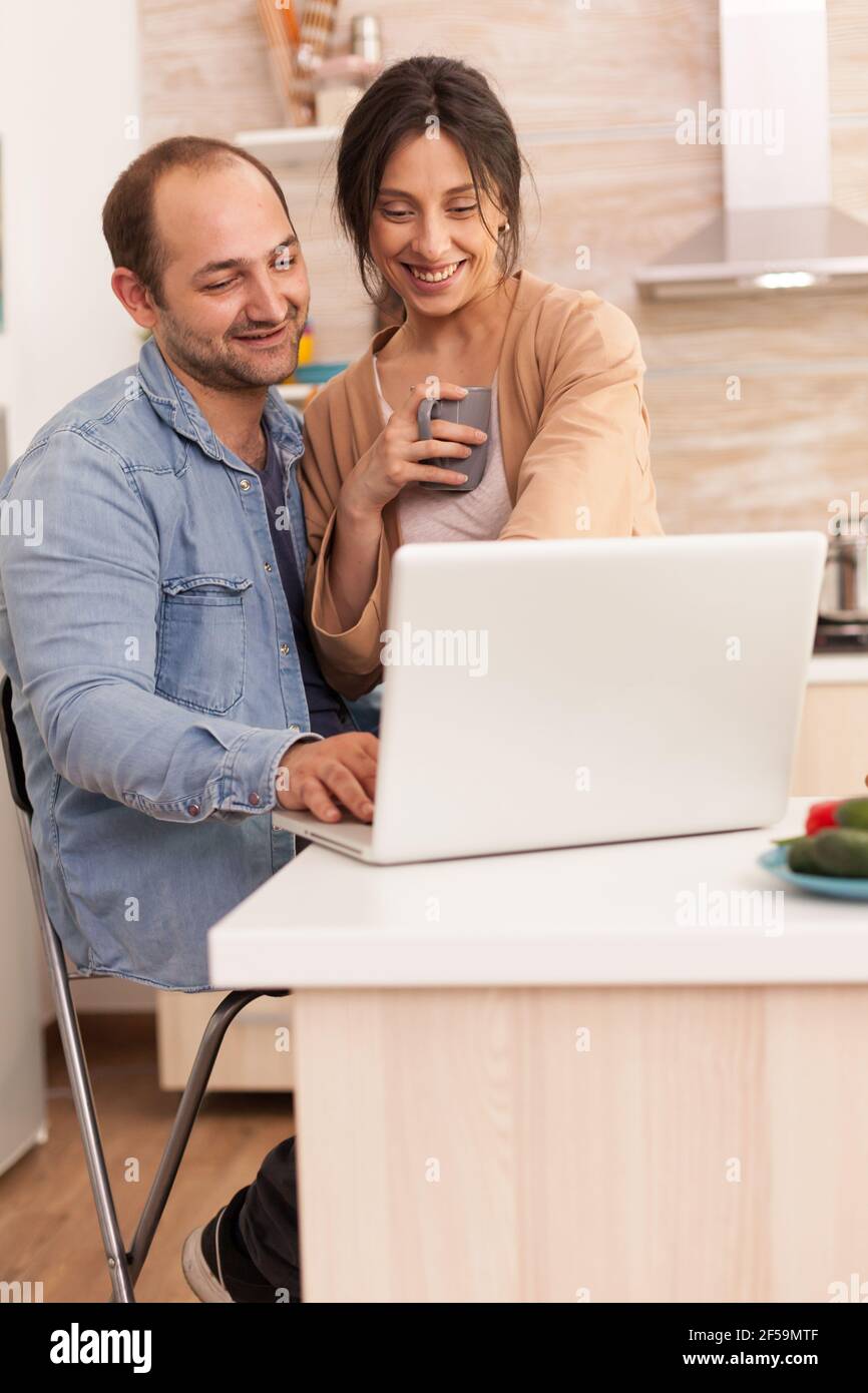Happy entrepreneur couple working on laptop in kitchen during morning ...