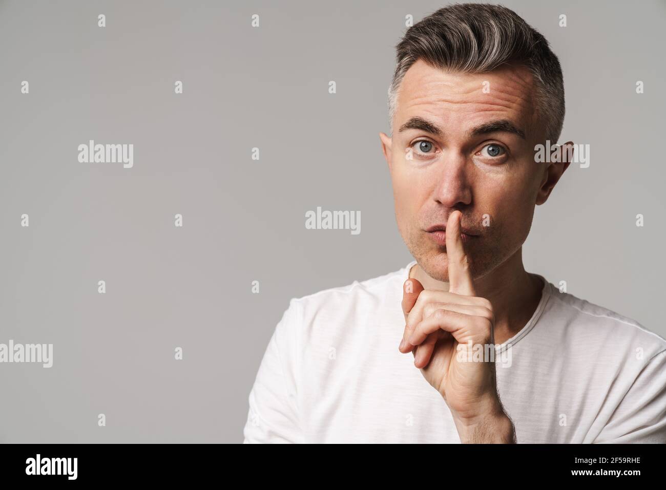 Serious man with finger on lips keeping a secret isolated over gray ...