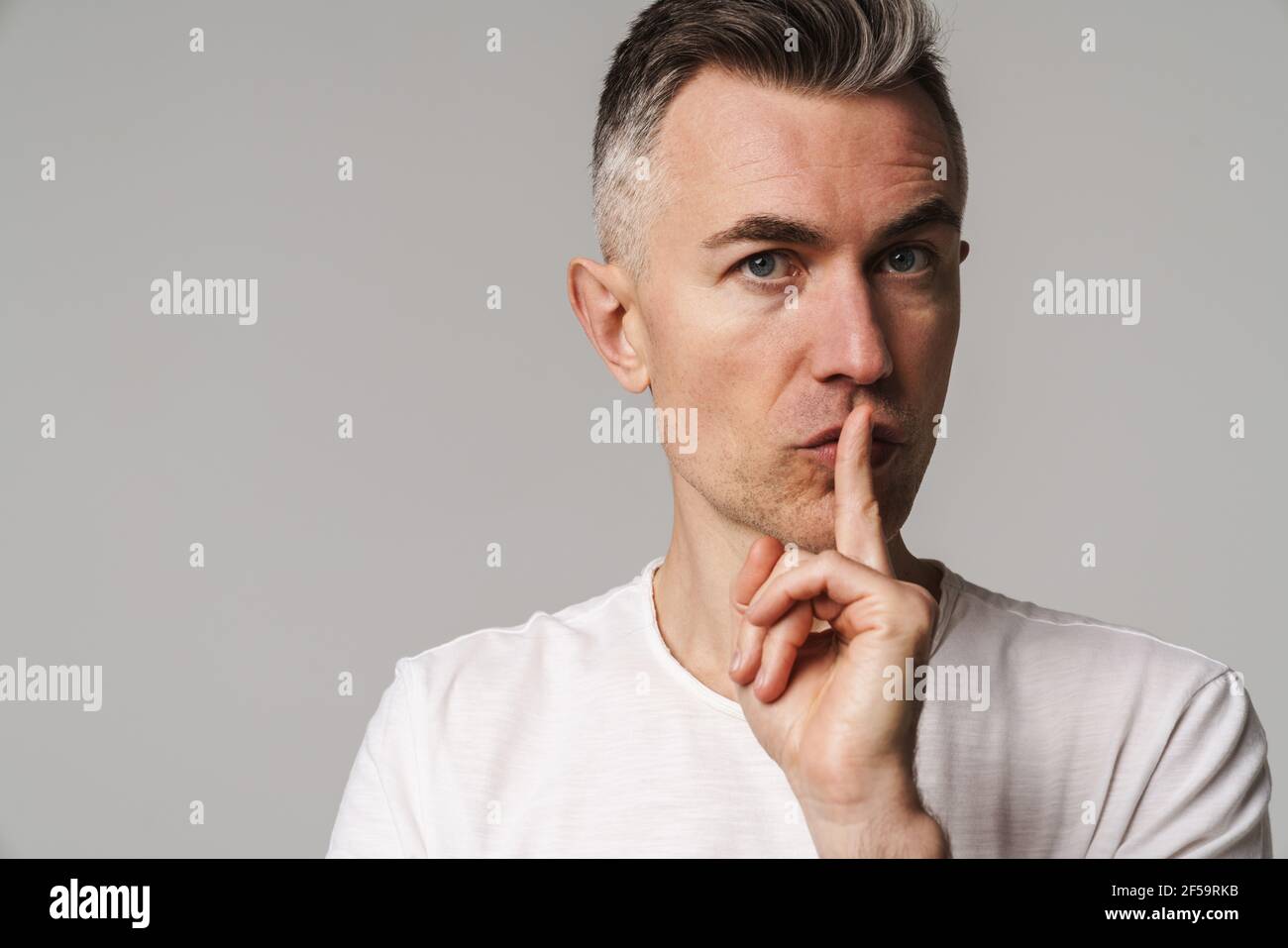 Serious man with finger on lips keeping a secret isolated over gray ...